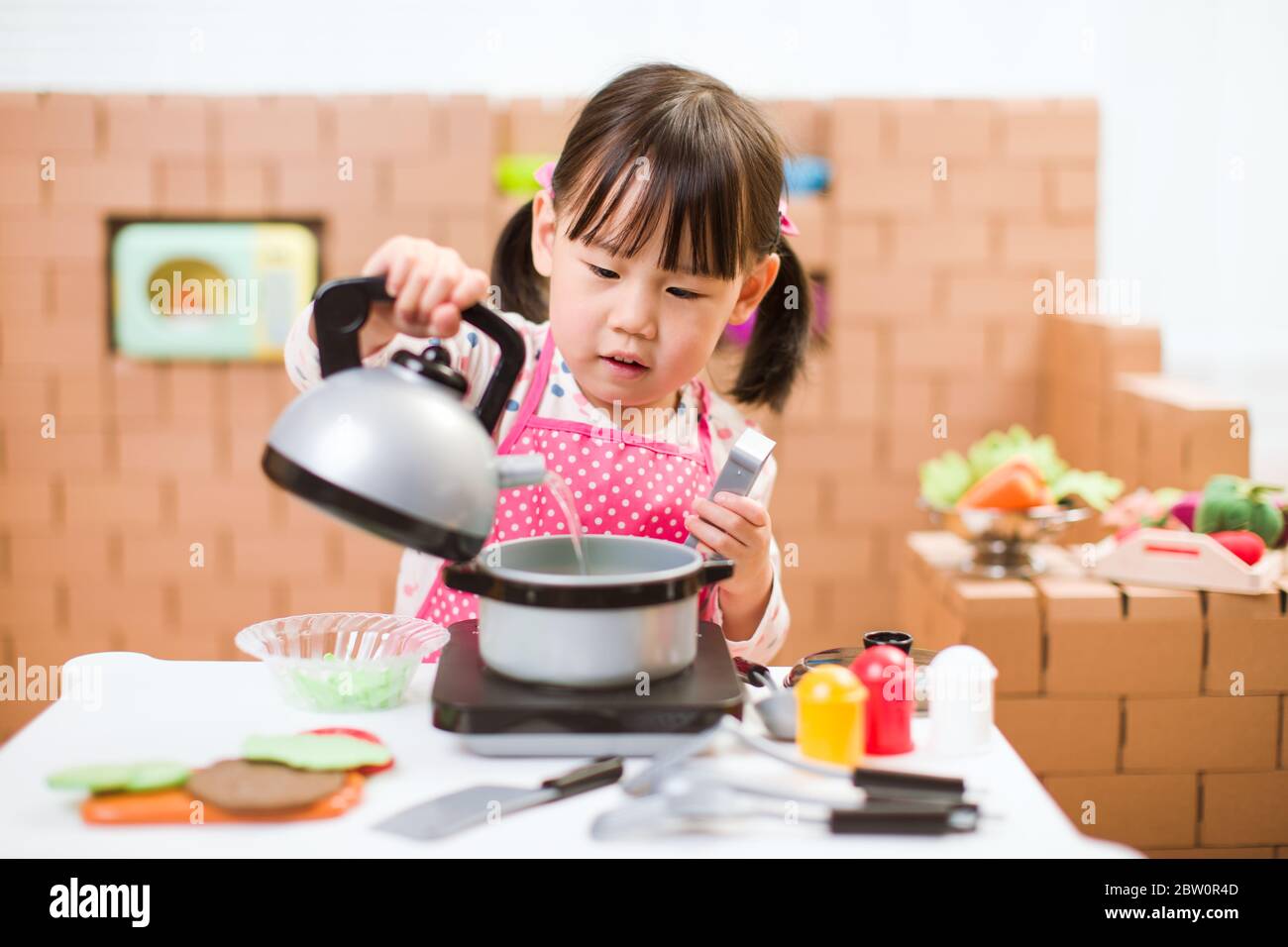 toddler girl pretend play food preparing role against cardboard blocks ...