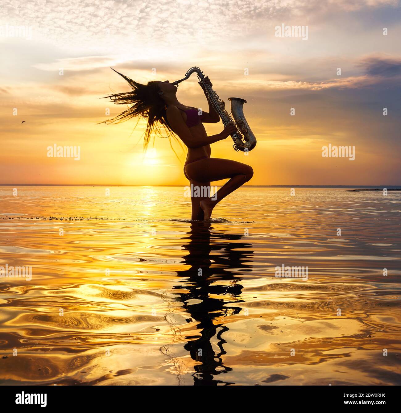 Silhouette of young shapely woman posing with saxophone in sea water ...