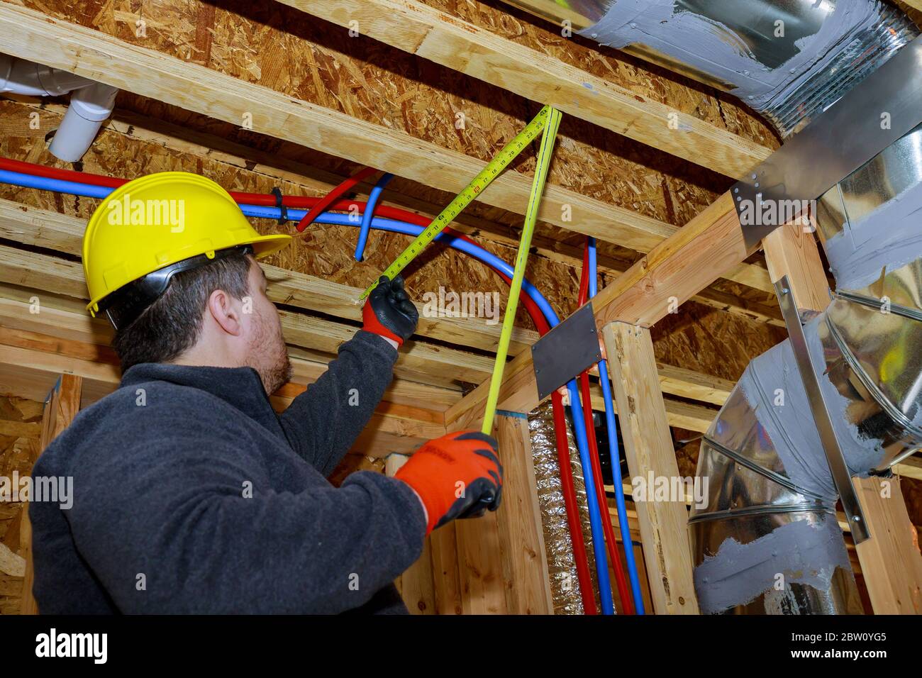 Male builder measuring plastic pipes with new home construction in hot ...