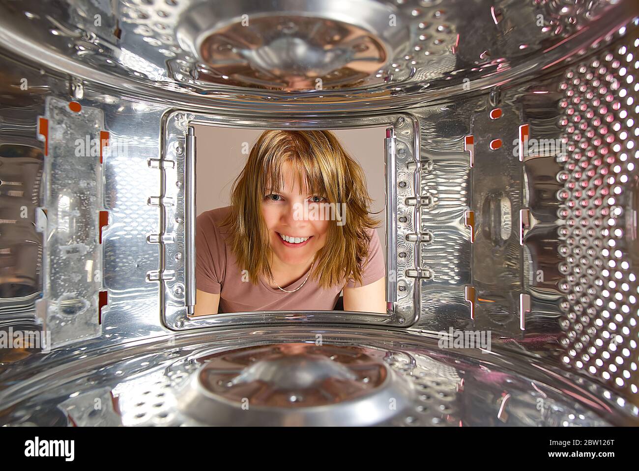 Woman looking into washing machine at laundromat without clothing ...