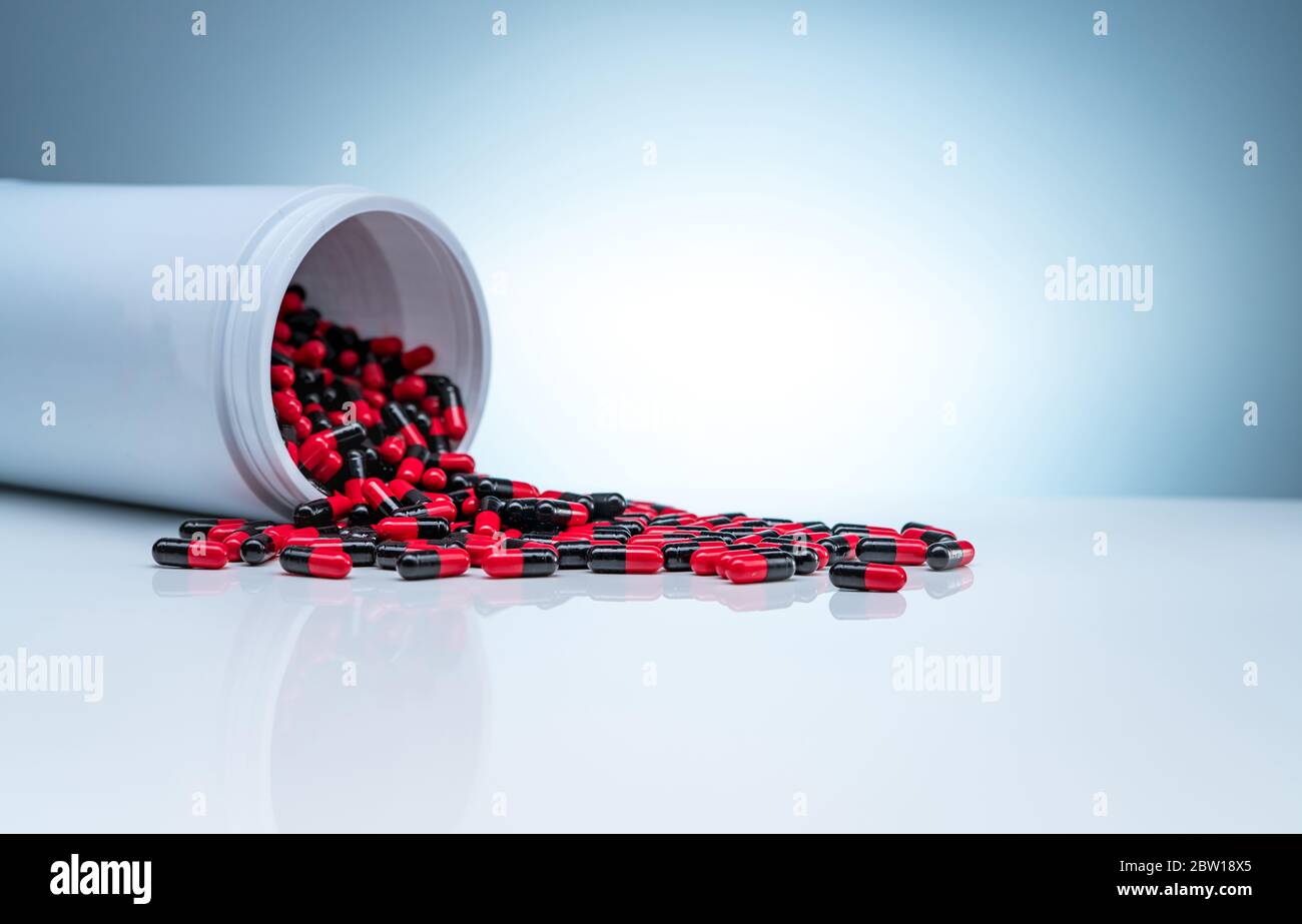 Red-black antibiotic capsule pills spread out of white plastic drug ...