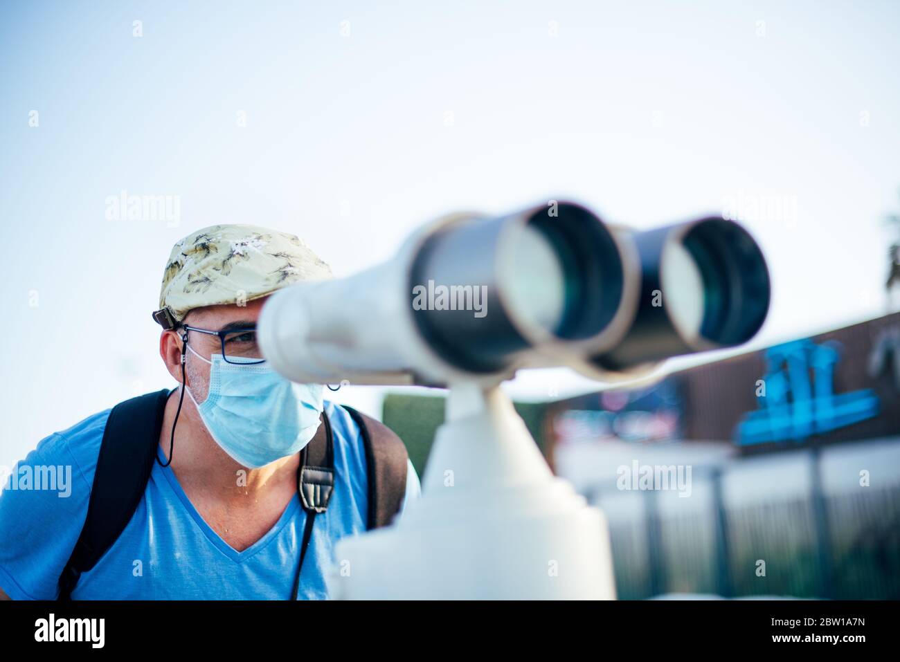 Tourist with mask and glasses looking through a binocular on the coast ...