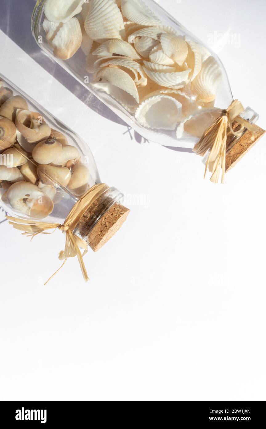 Two diagonal glass bottles filled with sea shells on white background ...