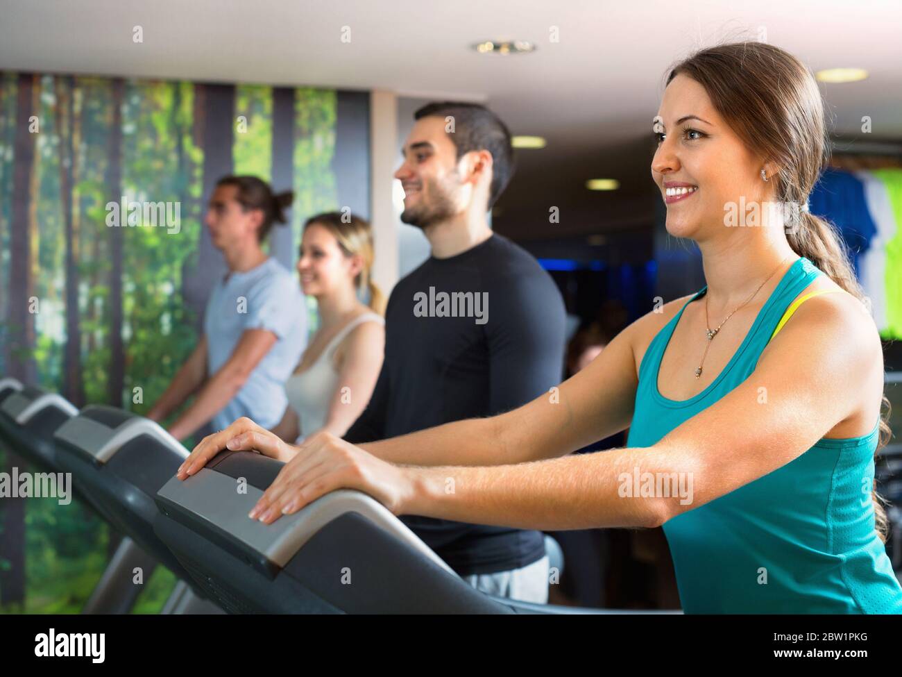 Group of smiling people doing cardio on treadmills in fitness club ...