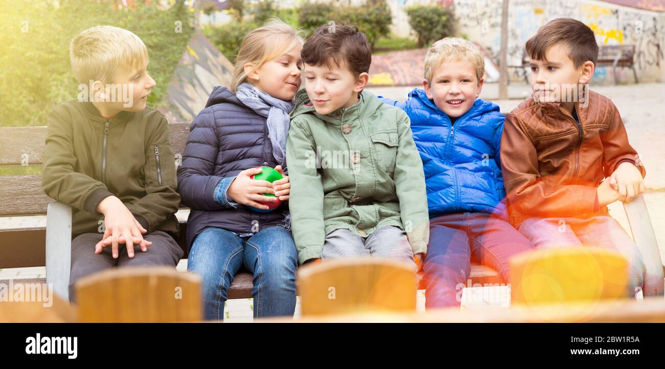 Group of cheerful children chatting while relaxing on bench on ...