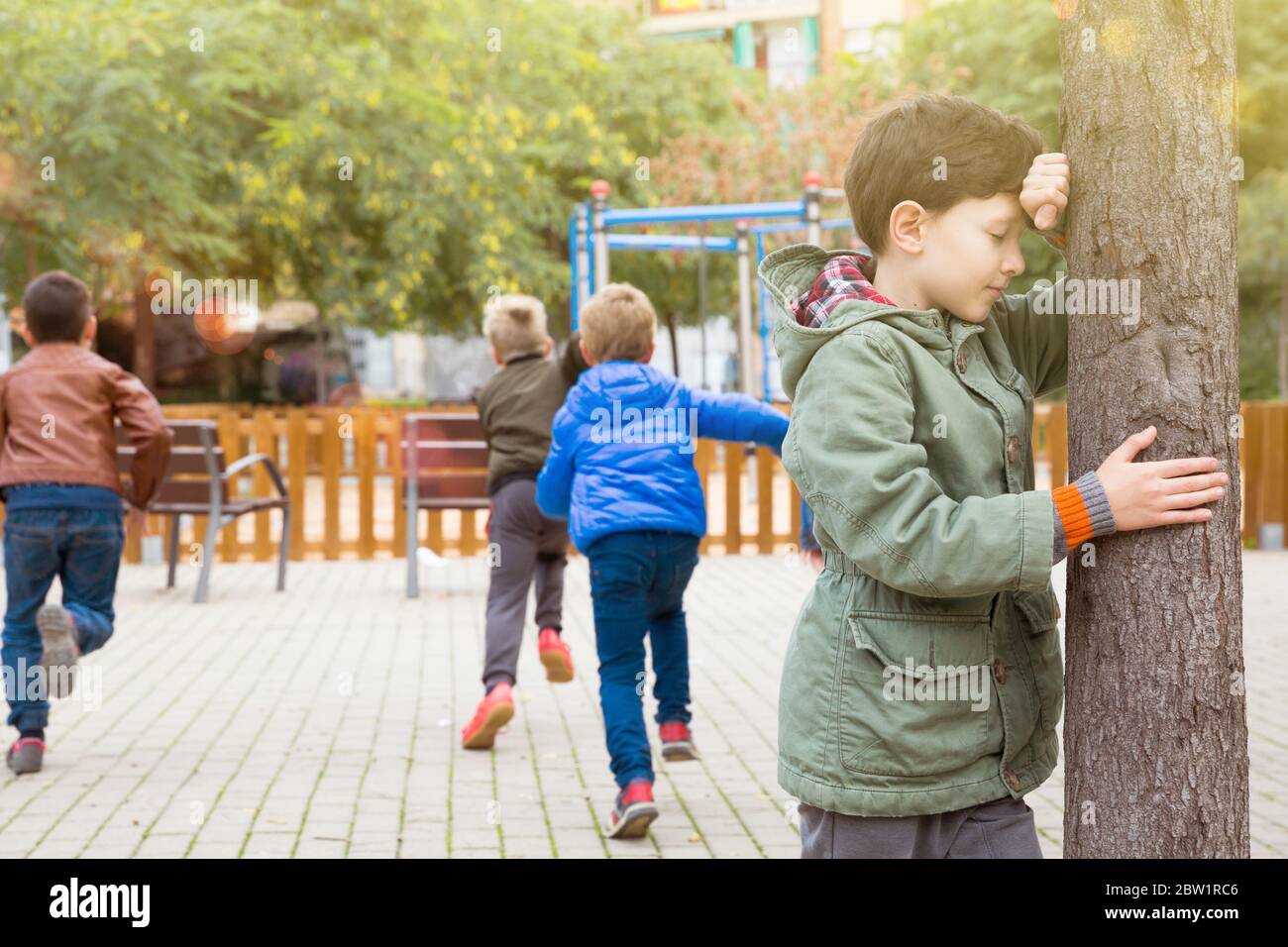 Children playing hide and seek outdoors. Boy standing near tree and ...