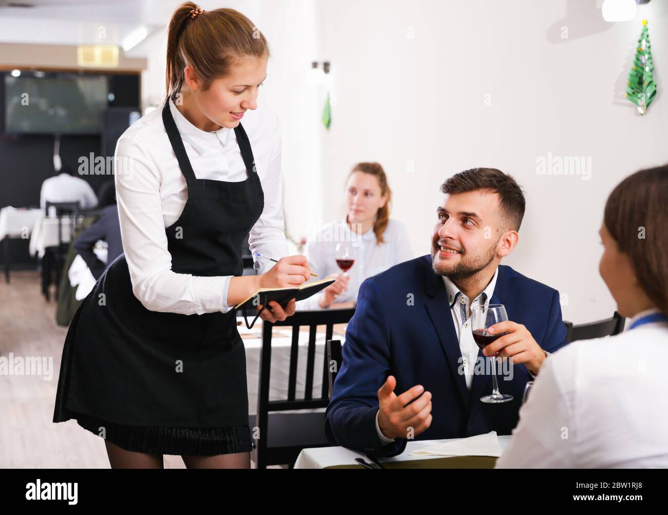 Welcoming female waiter is taking order from couple in restaurante ...