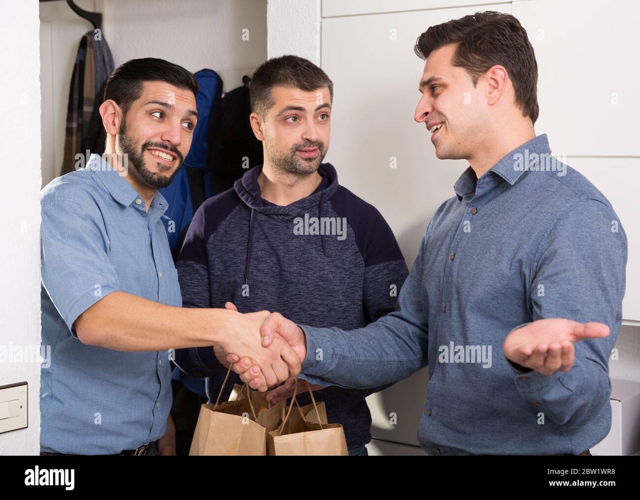 Two smiling men coming to visit their friend at home Stock Photo - Alamy