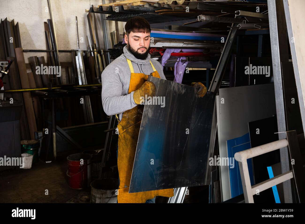 Confident young metalworker taking steel sheet from rack in mechanical ...