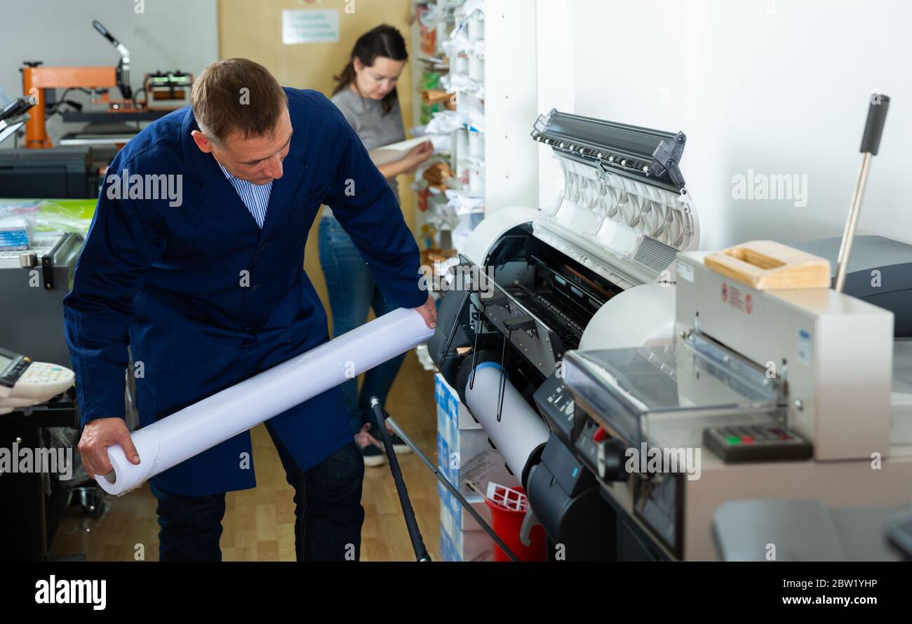Worker loads new roll of paper into the plotter Stock Photo - Alamy