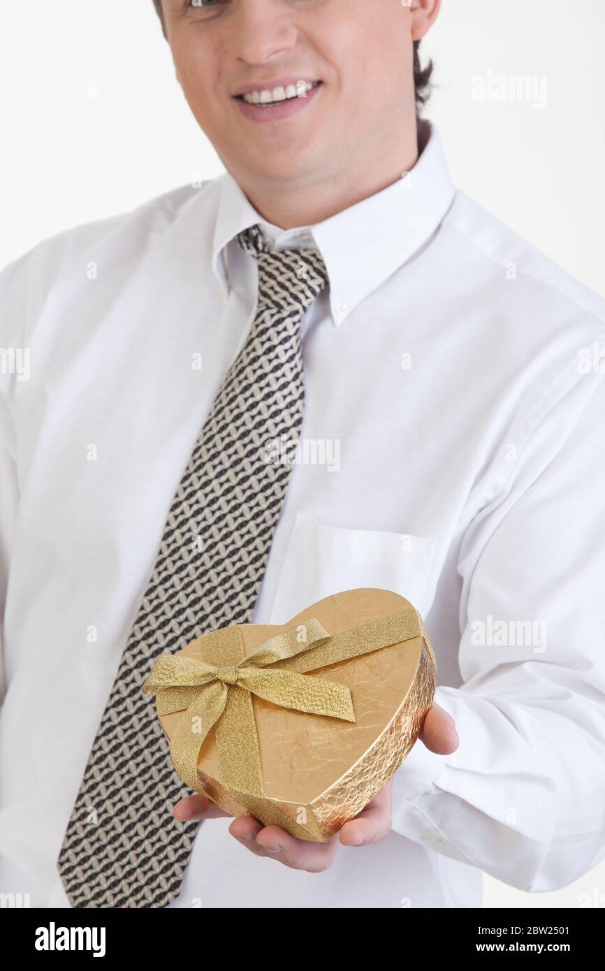 Young man with a heart shaped box in his hand on a white background ...