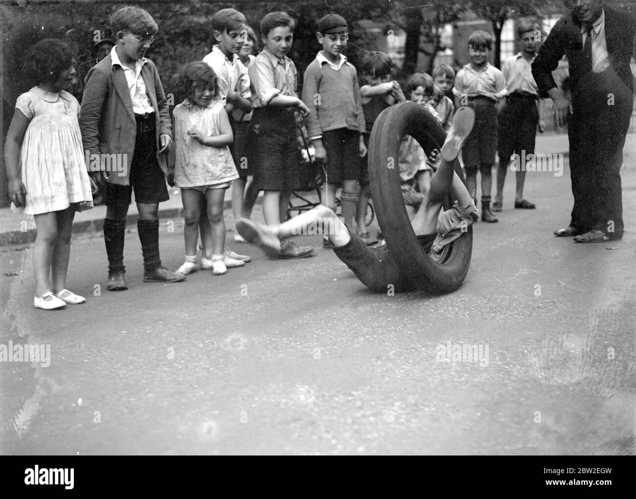 Children watching a boy rolling in a tyre. 1933 Stock Photo - Alamy