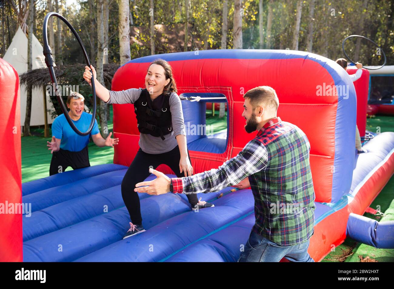 Cheerful woman playing tug of war with hoop on inflatable arena in ...