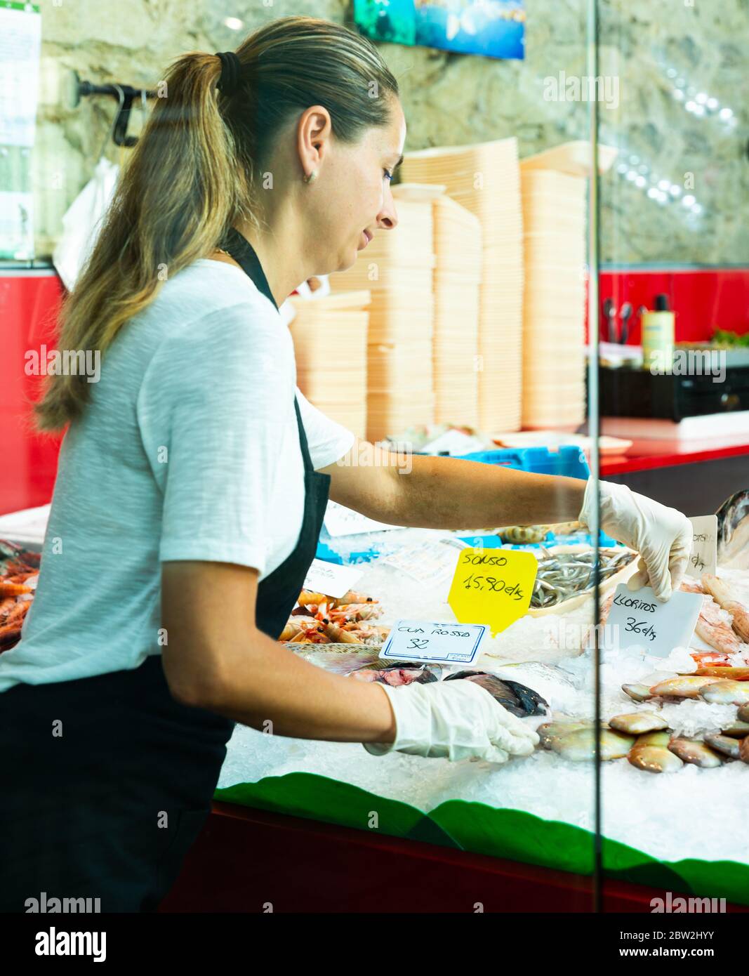 Female owner of fish shop arranging fresh raw seafoods on display case ...
