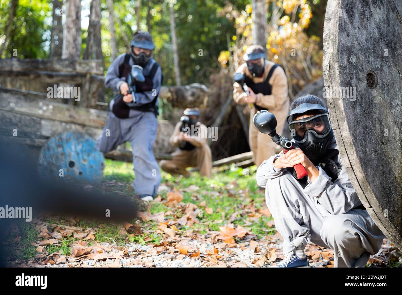 Men and women in protective uniform playing paintball on shooting range ...