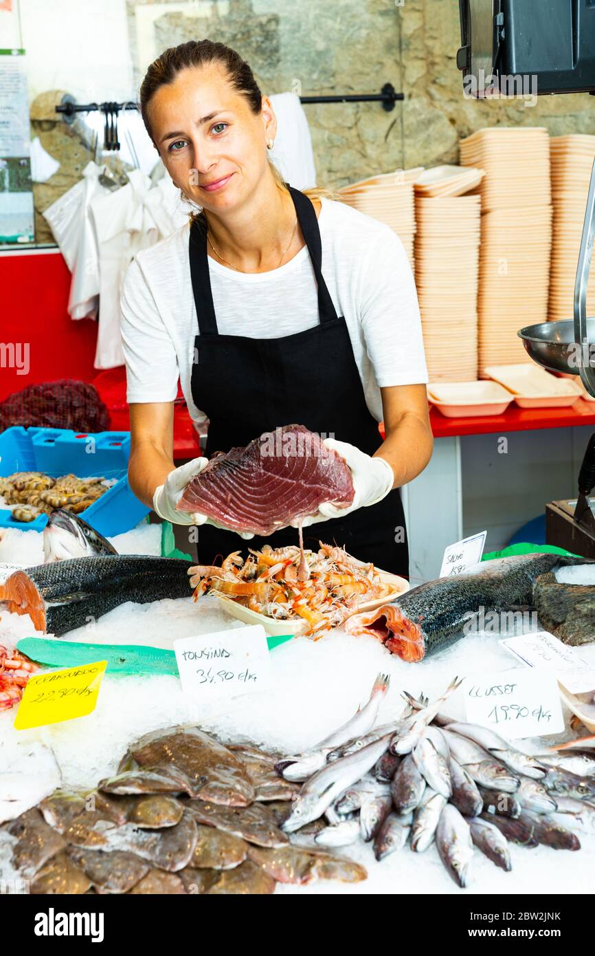 Confident female fishmonger standing behind seafood store counter ...