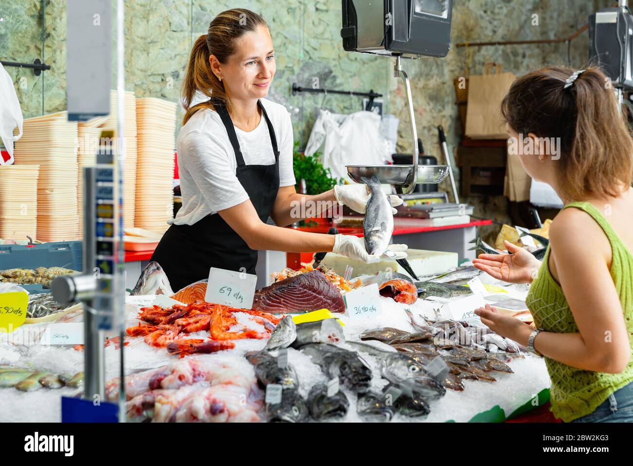 Portrait of friendly cheerful positive female fishmonger showing raw ...