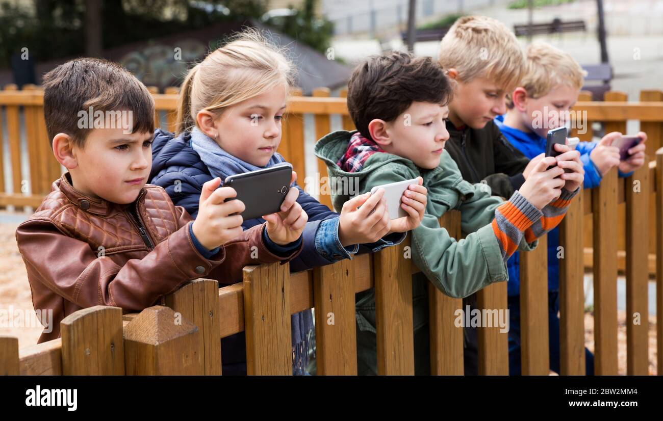 Interested kids playing with smartphones while standing near wooden ...