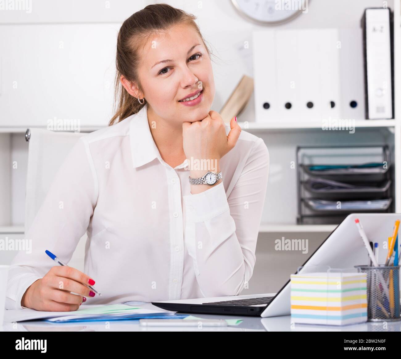 Adult female is posing while working behind laptop in the office Stock ...
