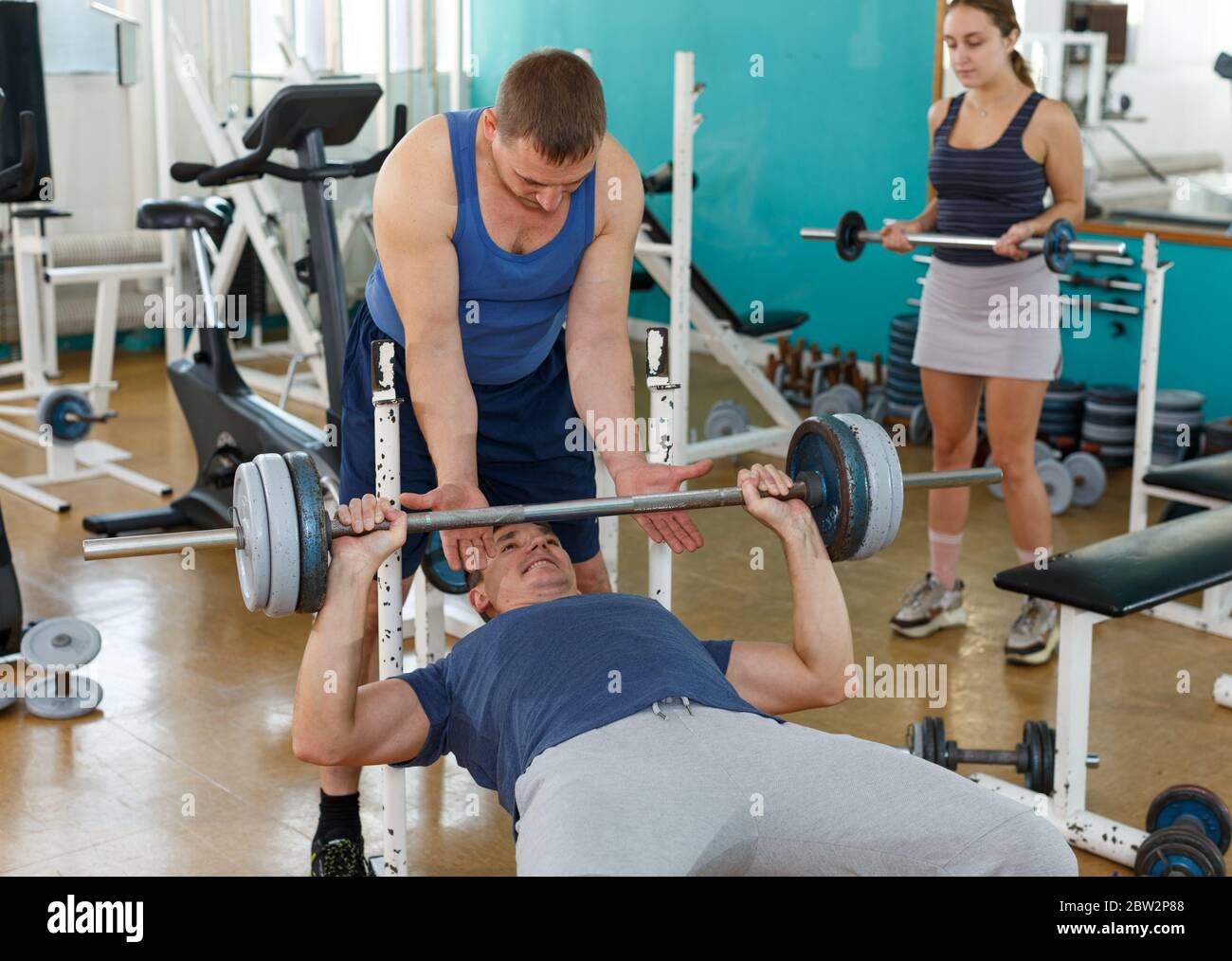 Sports instructor helping man doing exercises with barbell in sport ...