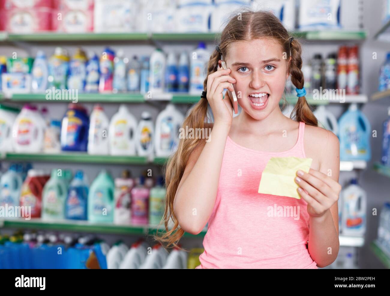 Teenage girl choosing goods with shopping list and talking by phone in ...