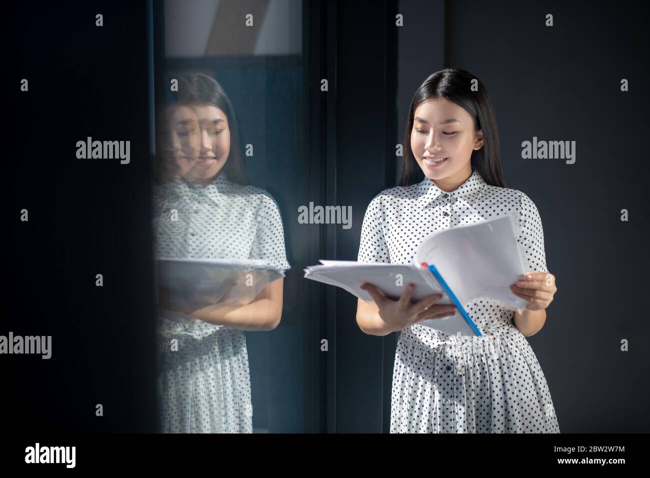 Young brunette female standing near the window, looking through ...