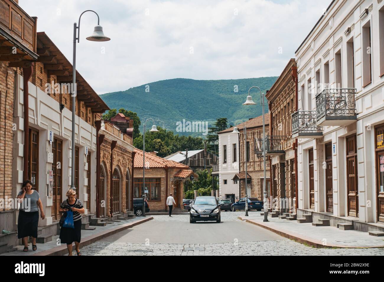 Two women walk and a car drives down an ornate street in the city of ...