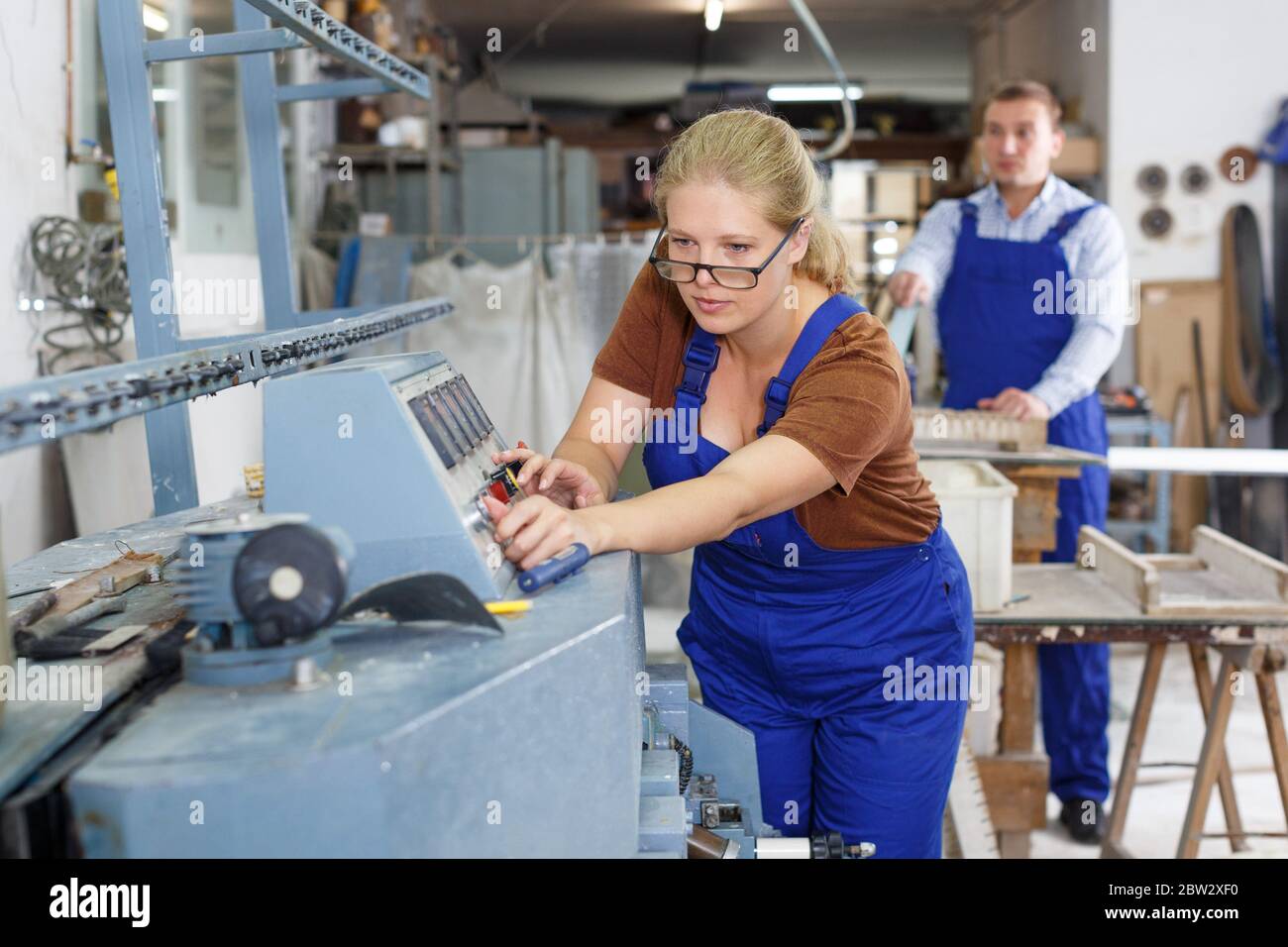 Confident female glazier working on glass straight line bevelling ...