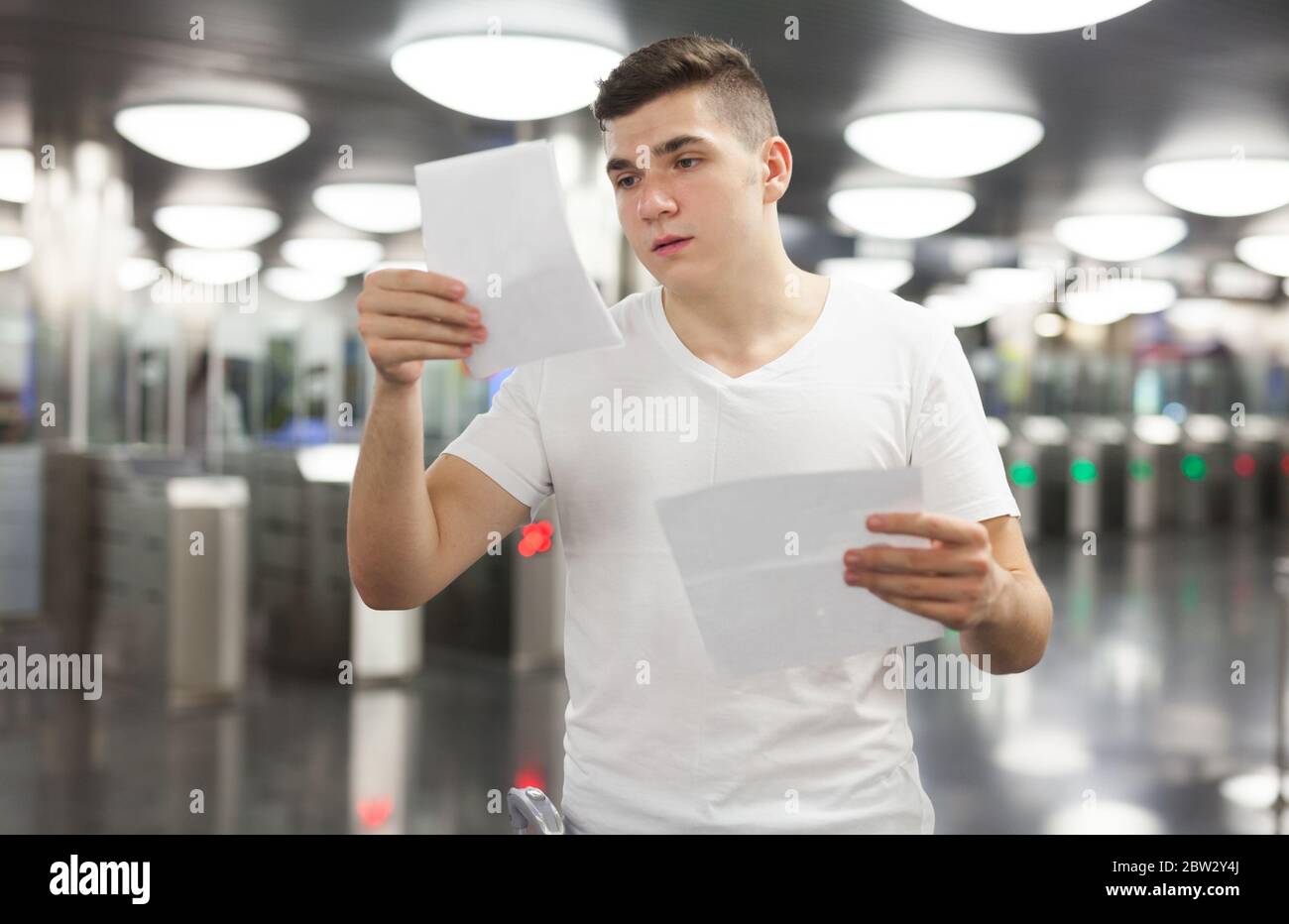 Young male passenger in casual clothing with baggage holding papers on ...