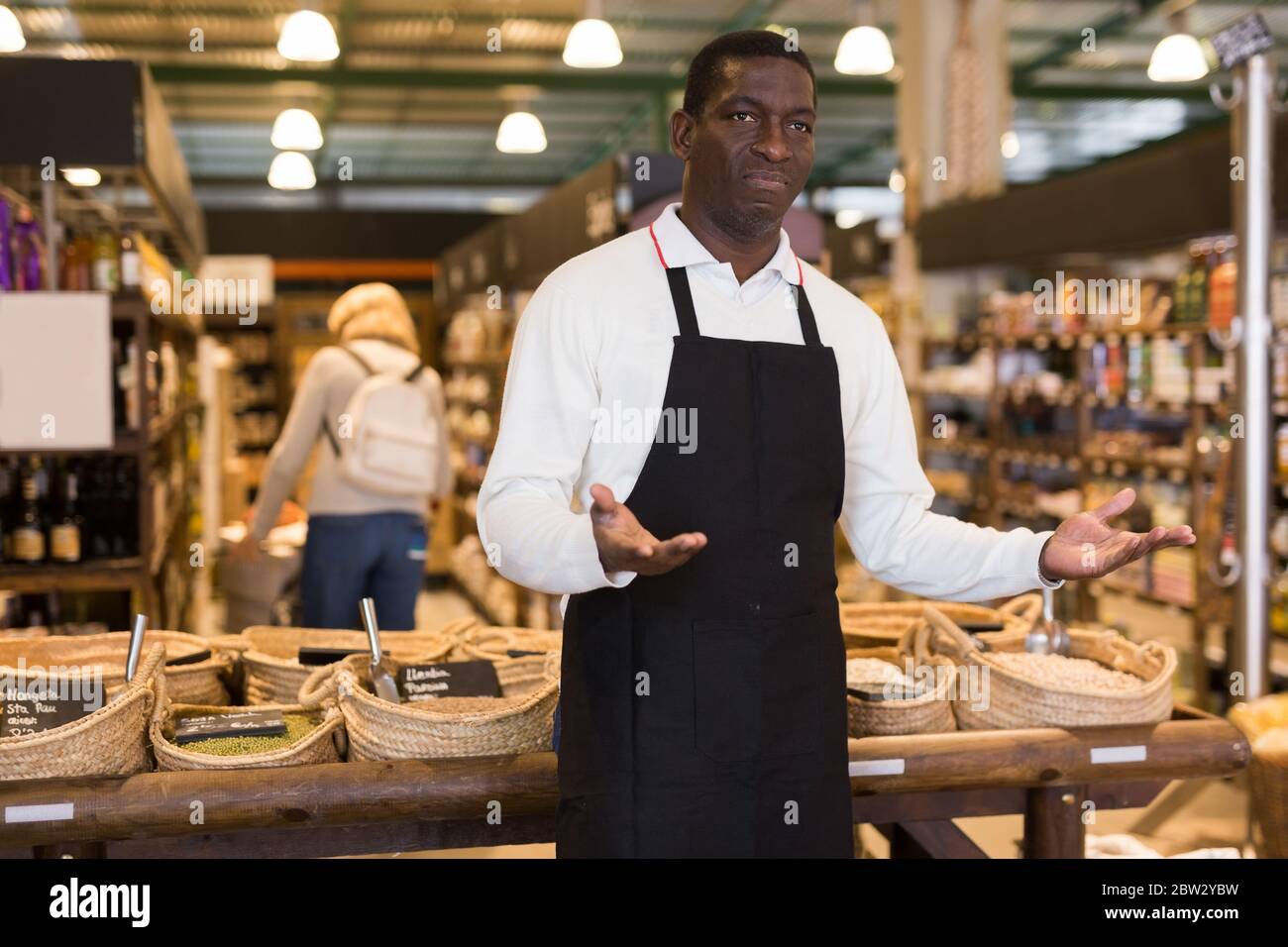 Portrait of polite African American salesman inviting to grocery store ...