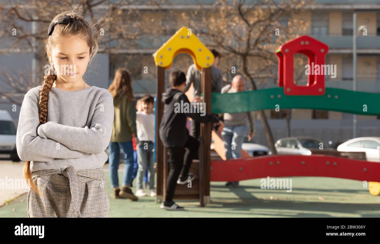 Portrait of upset little girl standing in front of children playing ...