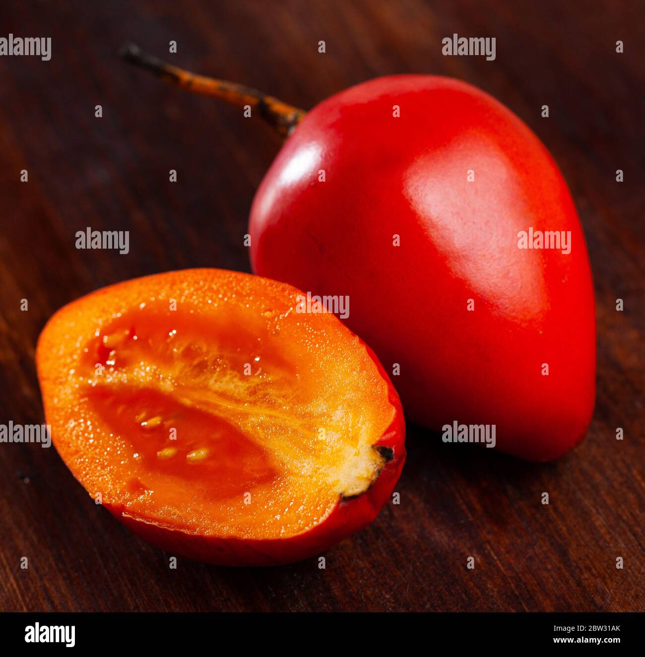 Whole and half fresh red tamarillo on wooden table. Healthy vegetarian ...