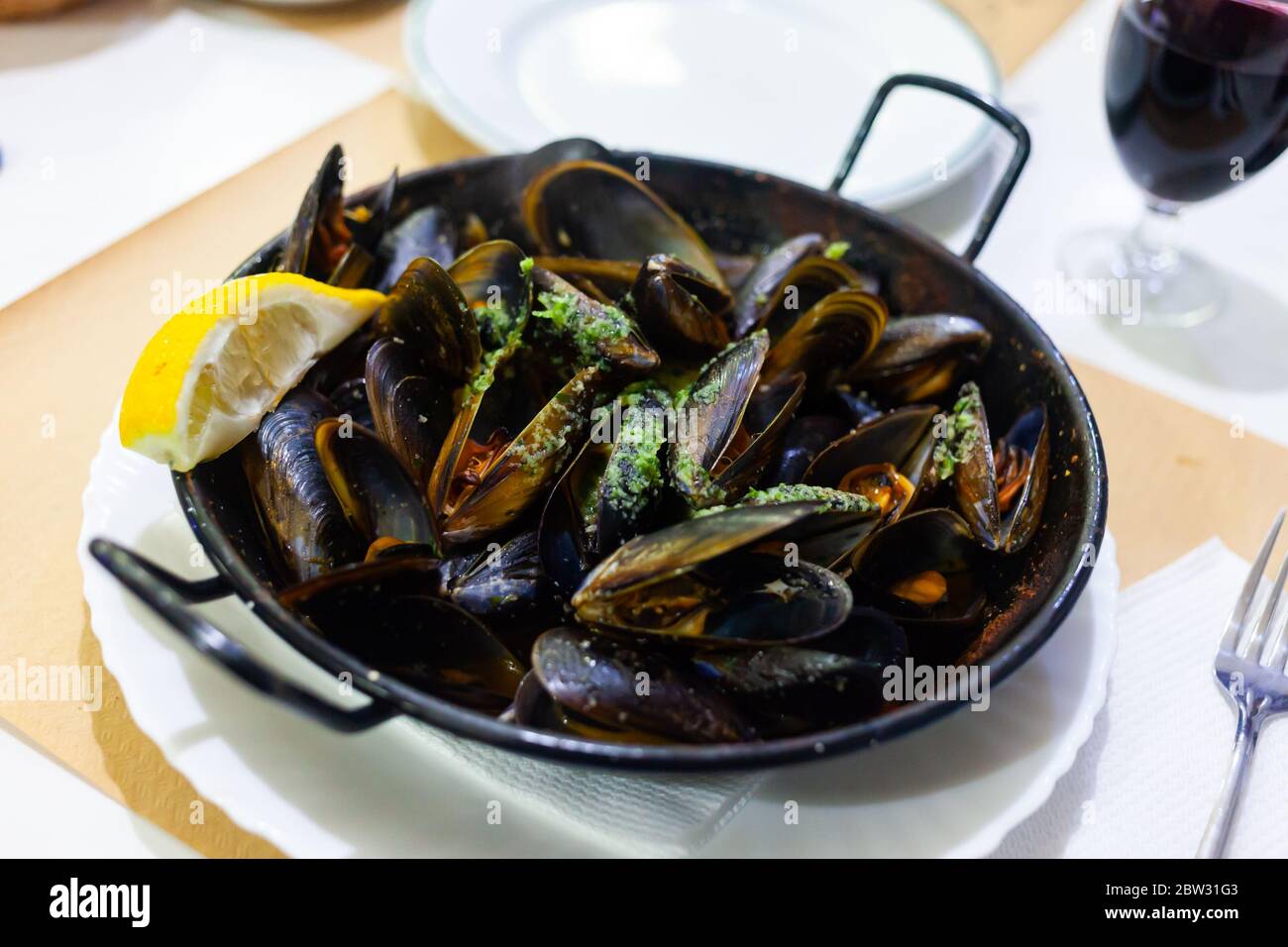 Image of delicious mussels on a frying pan with lemon at table Stock ...