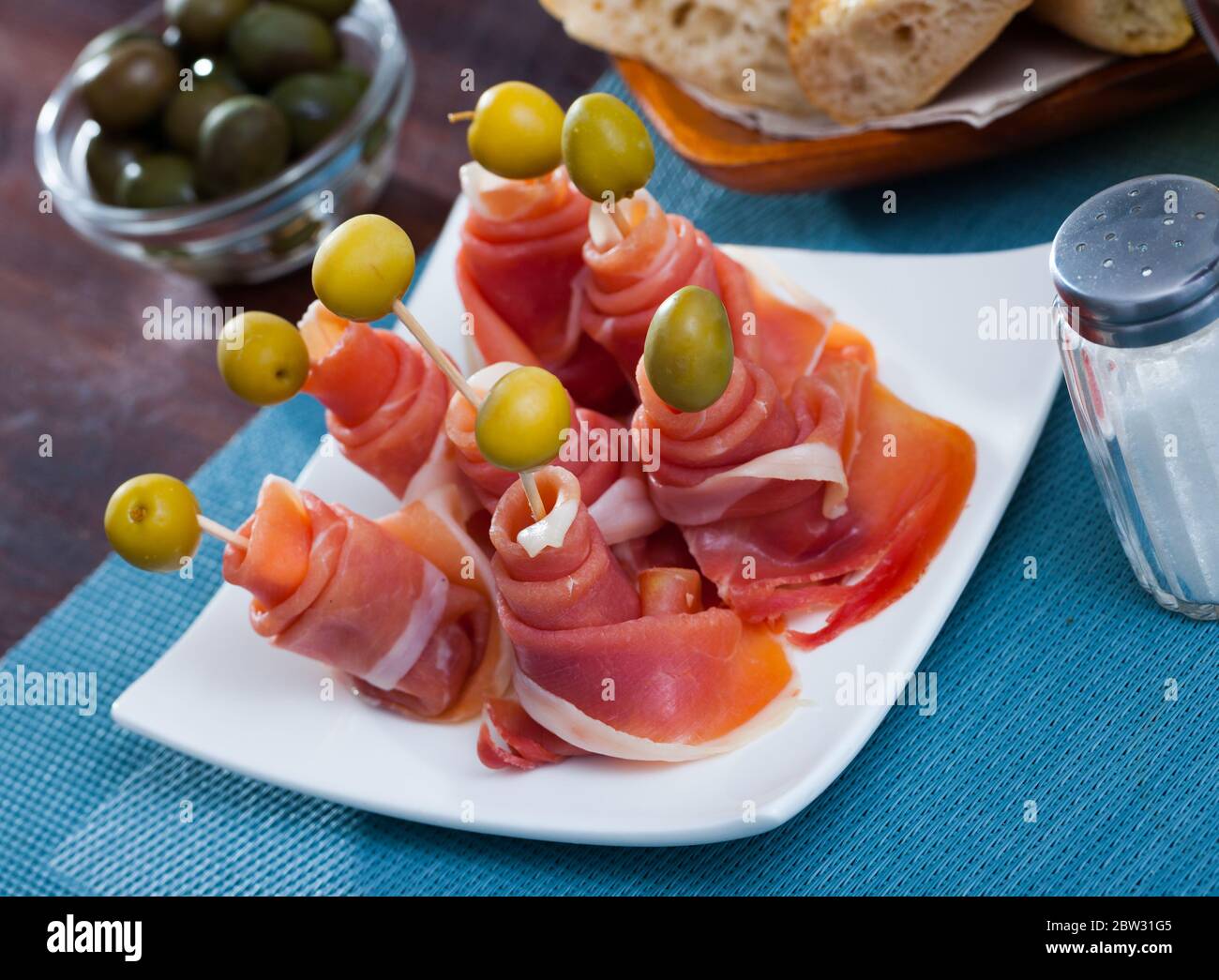 Rolls of delicate cured jamon slices served on white plate with olives ...