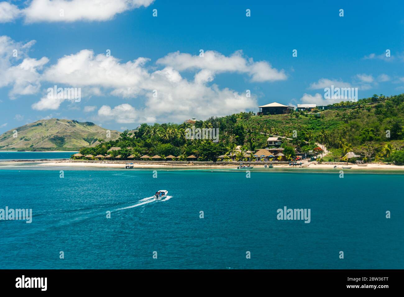 Motor boat driving towards a tropical island in deep turquoise water in ...