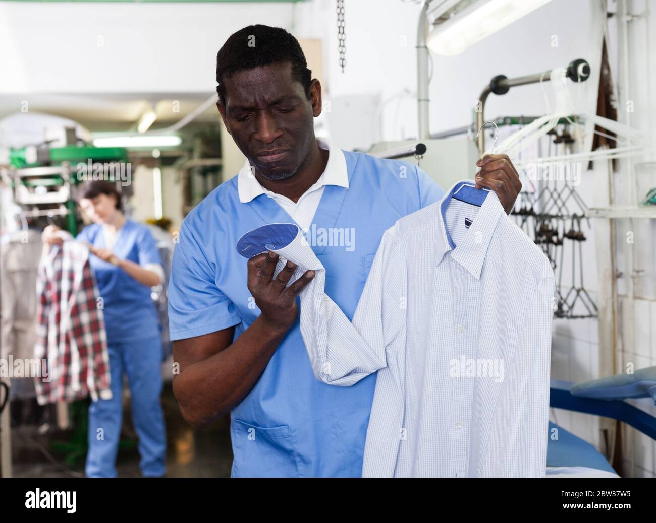 Focused African-American man working in modern laundry, checking ...