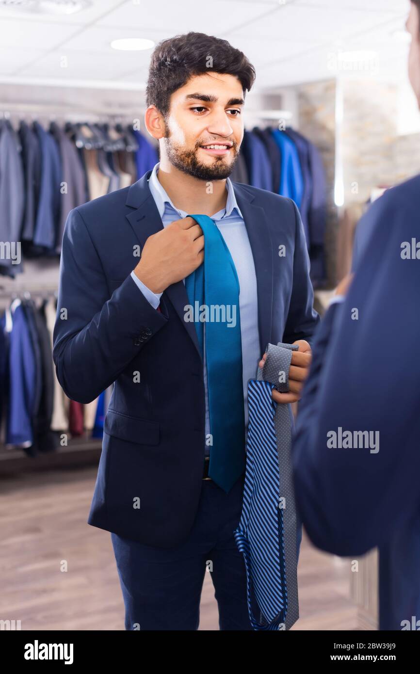 Customer is picking up tie for jacket in front of the mirror in men's ...