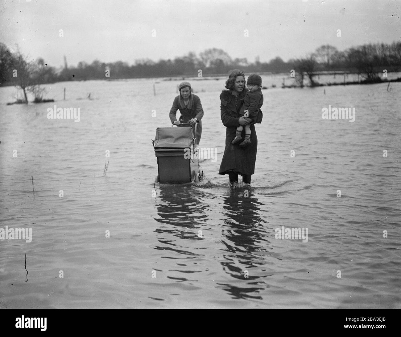 Floods in Berkshire . Two girls with a pram and child walking in flood ...