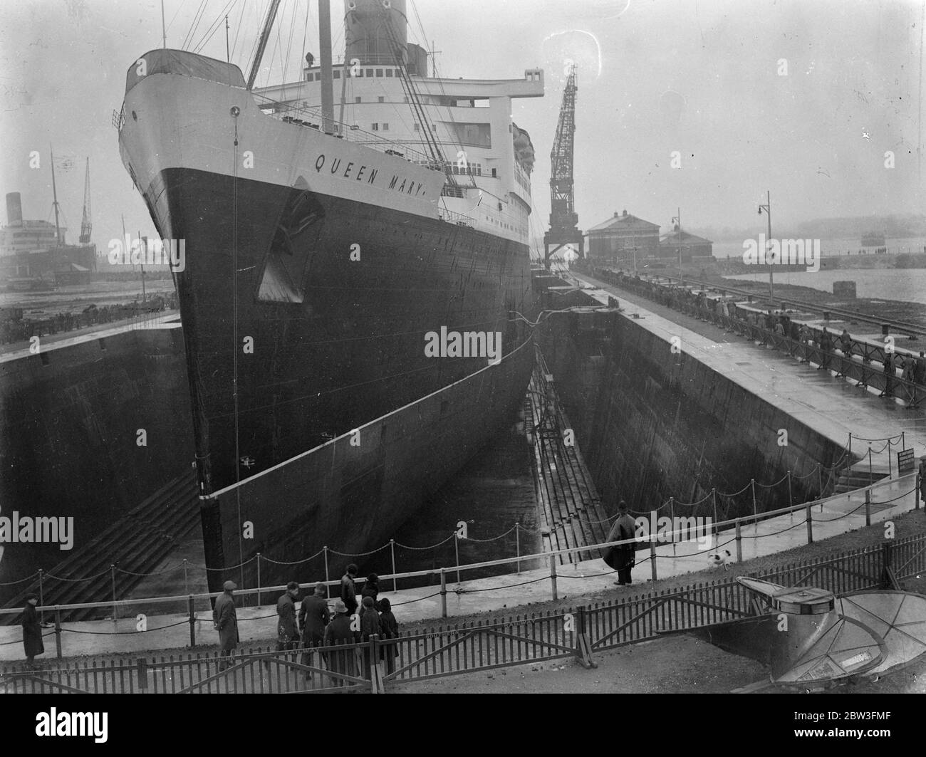 Thousands inspects the Queen Mary in dry dock at Southampton . Dwarfed ...