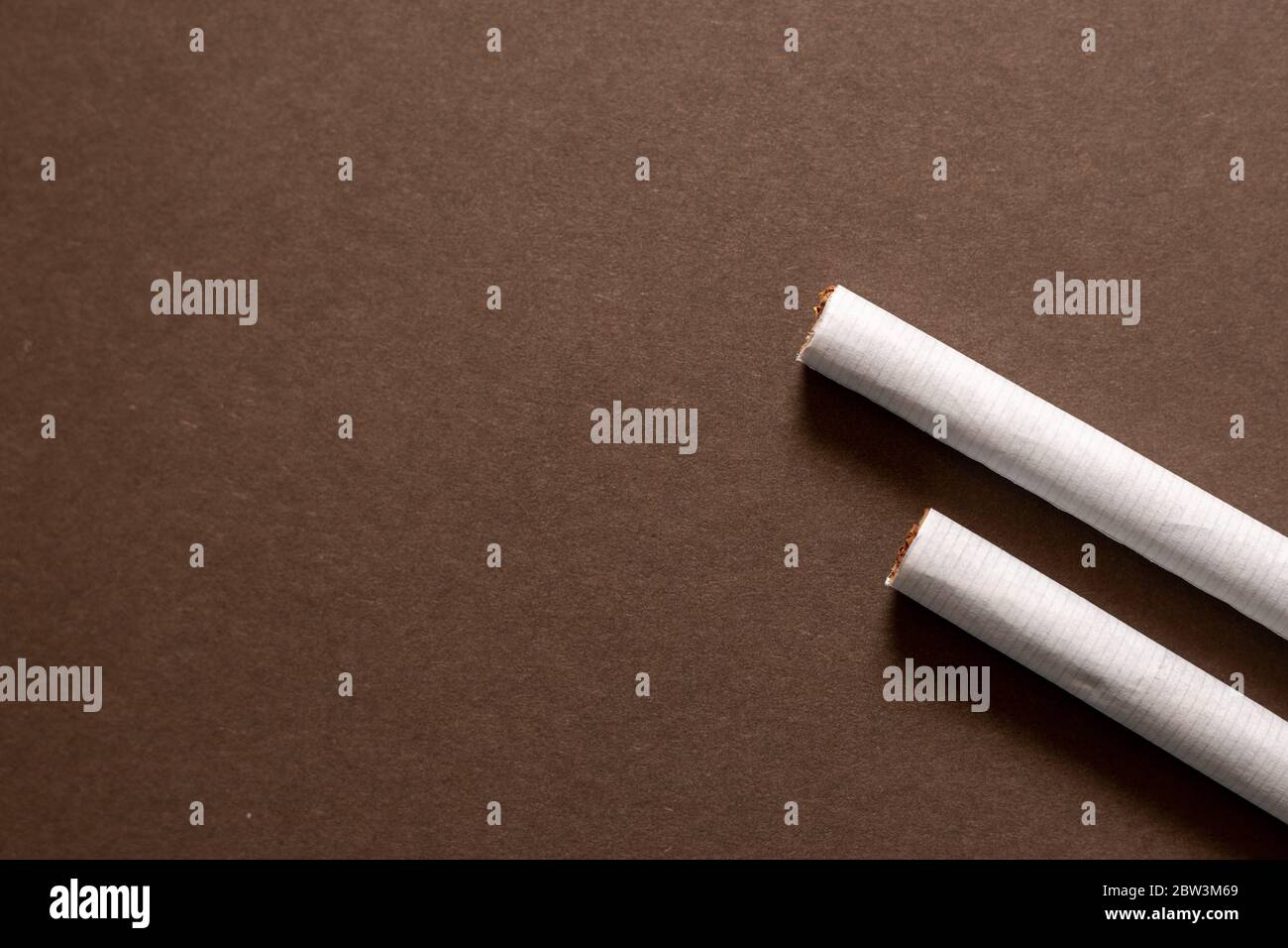 Two cigarette end laying flat on a brown background. Left area empty ...