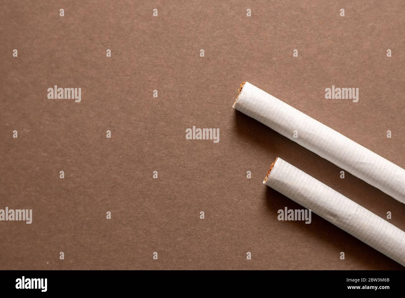 Two cigarette end laying flat on a brown background. Left area empty ...