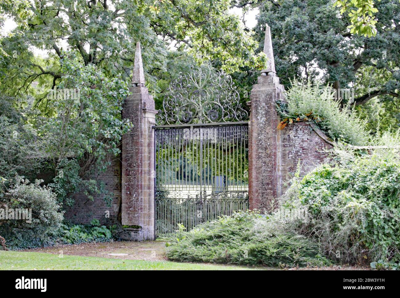 Old wrought iron gates mounted between two tall slim brick gate posts ...