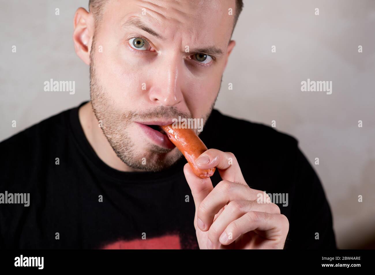 unshaven man eating a sausage, holding it with his hand Stock Photo - Alamy