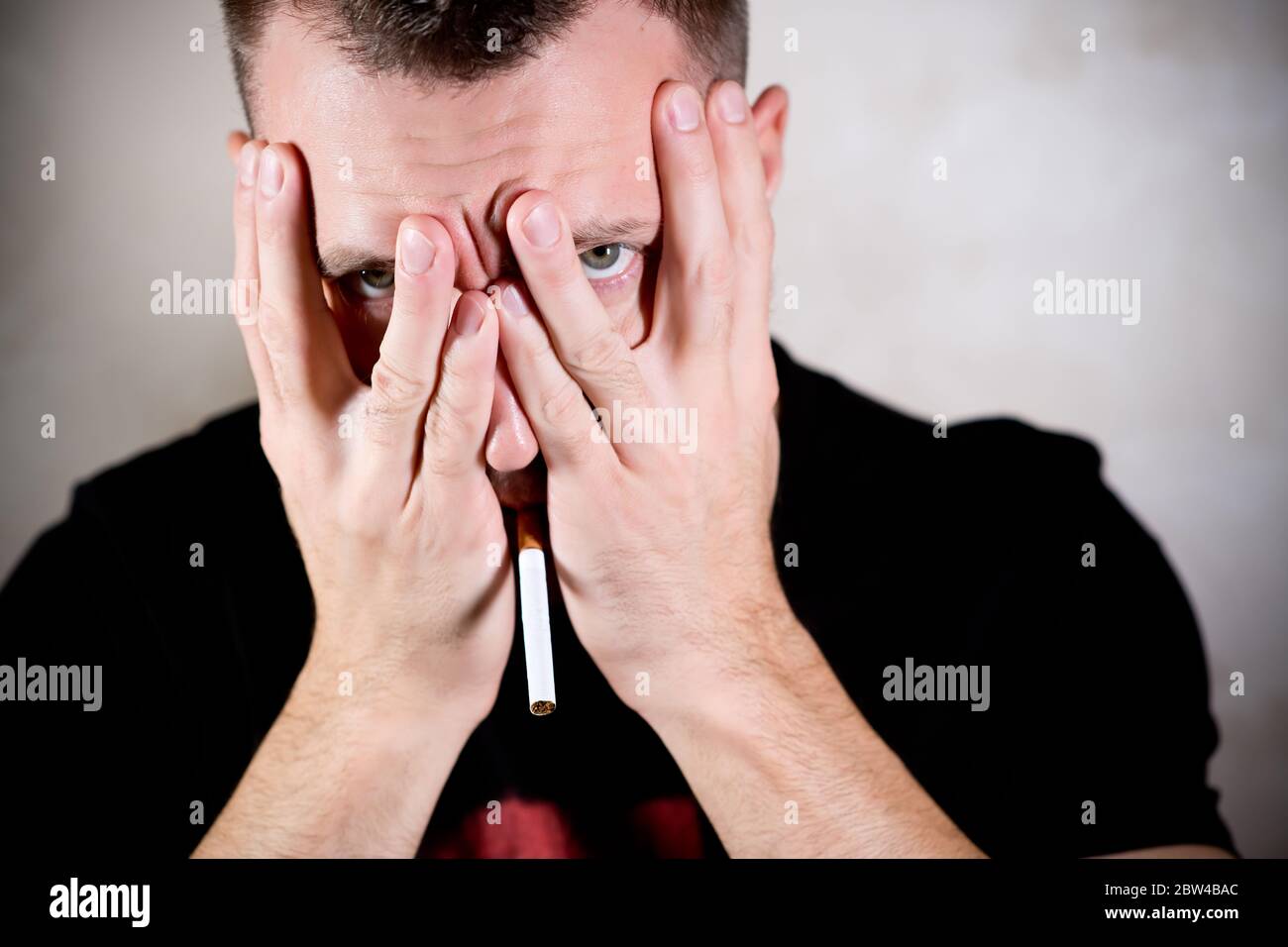 secret smoker with a cigarette in his mouth shamely covers his face ...