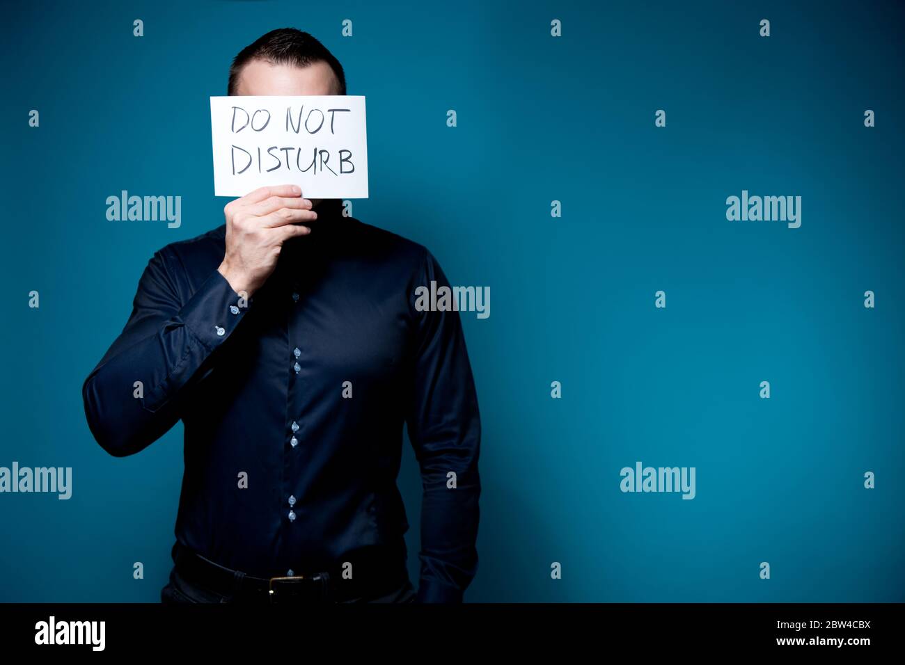 a man in a blue shirt covers his face with a do not disturb sign Stock ...