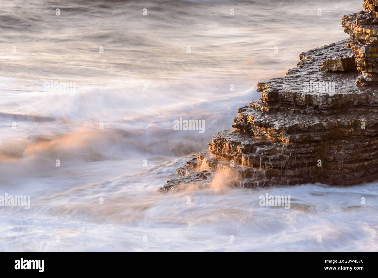Waves crashing over a tiered rock formation Stock Photo - Alamy