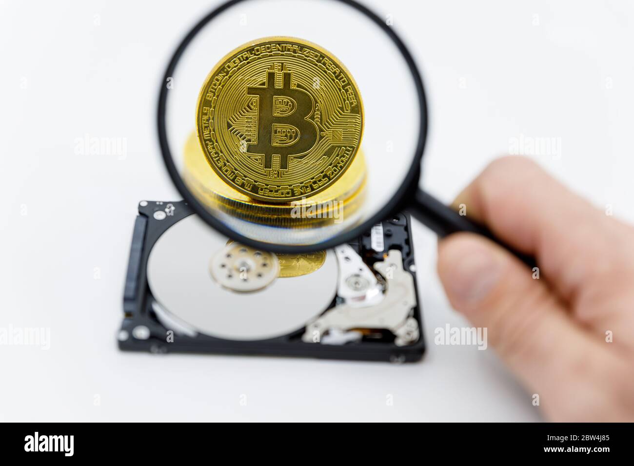 Magnifying glass over a gold bitcoin token on top of an open hard drive ...