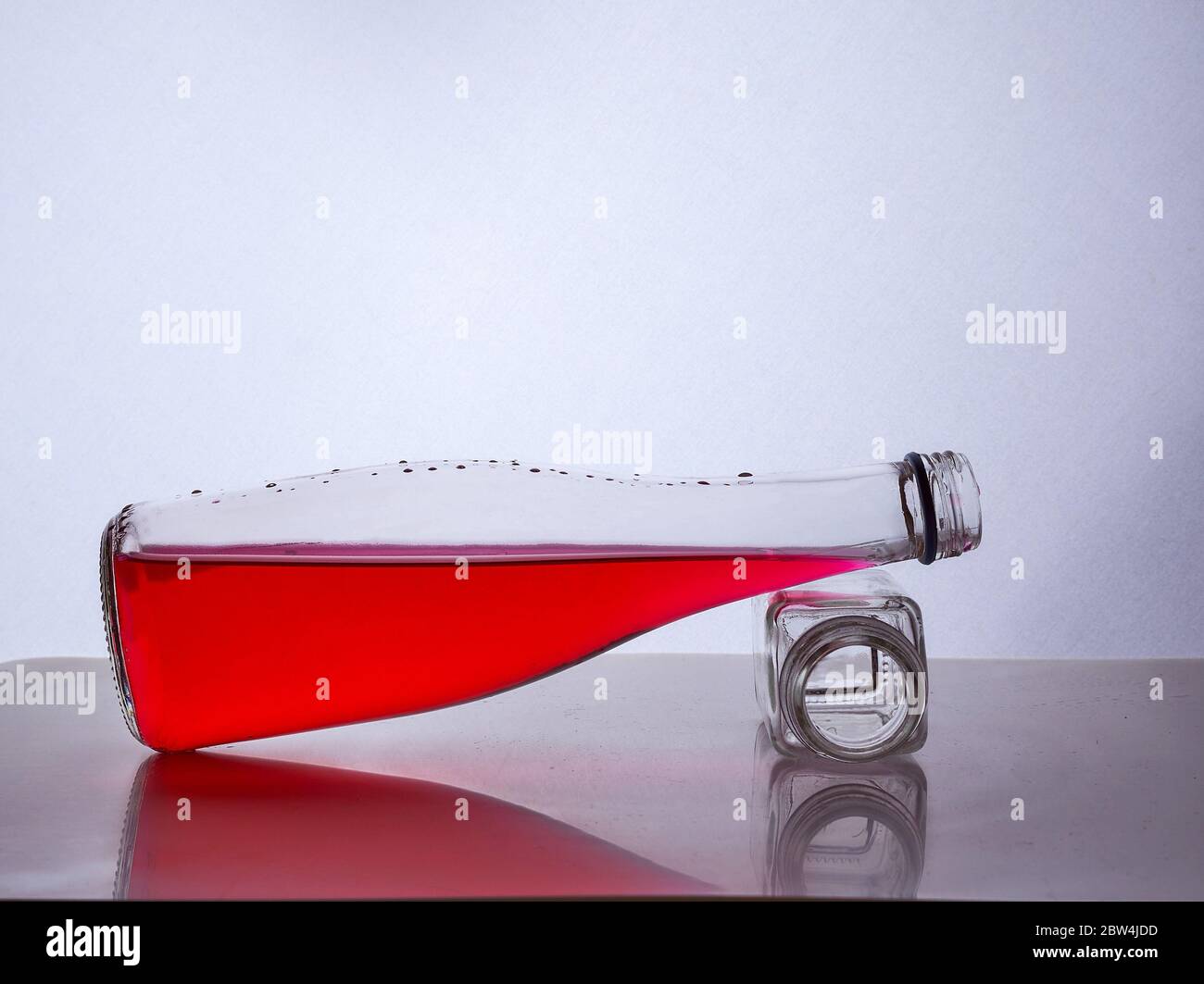 glass bottle with red liquid inside lies on a small bottle of white ...