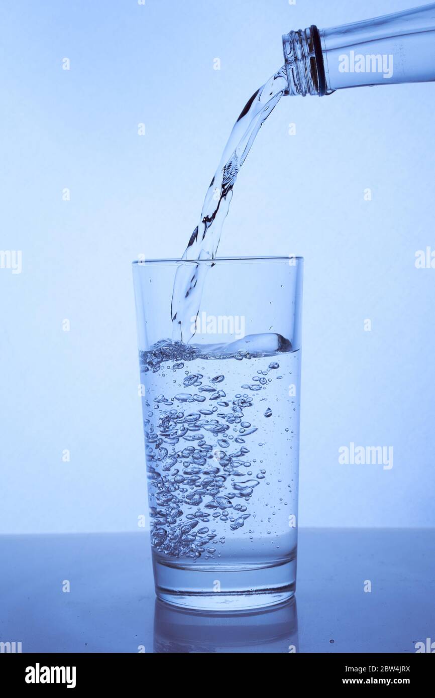 fresh clean water is poured from a bottle into a glass cup. Light ...