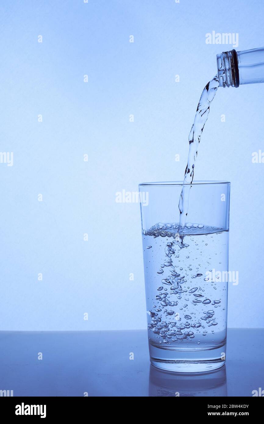 fresh clean water is poured from a bottle into a glass cup. Light ...